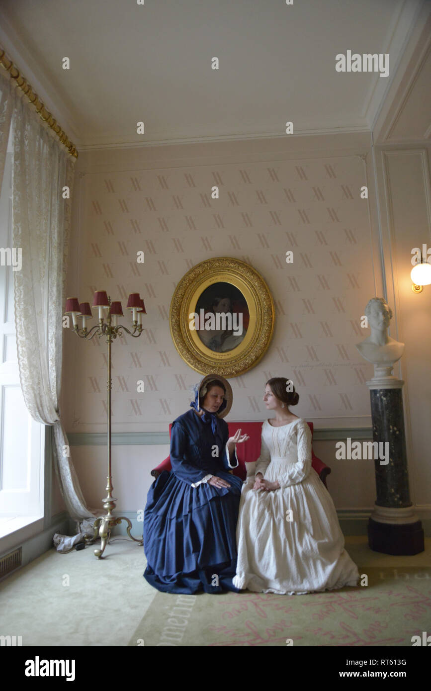Two Women in Victorian dresses sit and chat in a formal parlour at ...