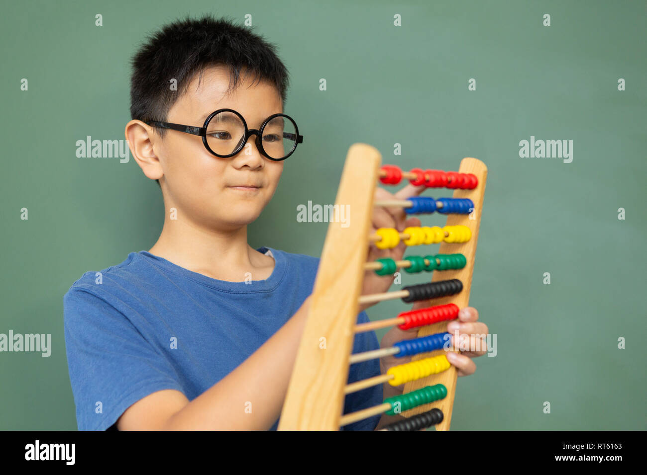 Boy learning math with abacus against green chalkboard in a classroom ...