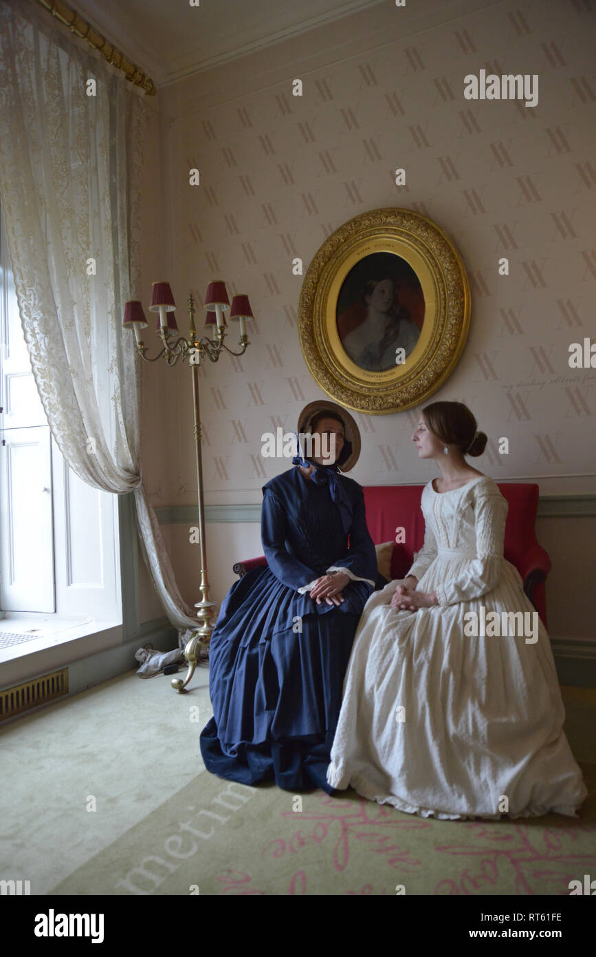 Two Women in Victorian dresses sit and chat in a formal parlour at ...