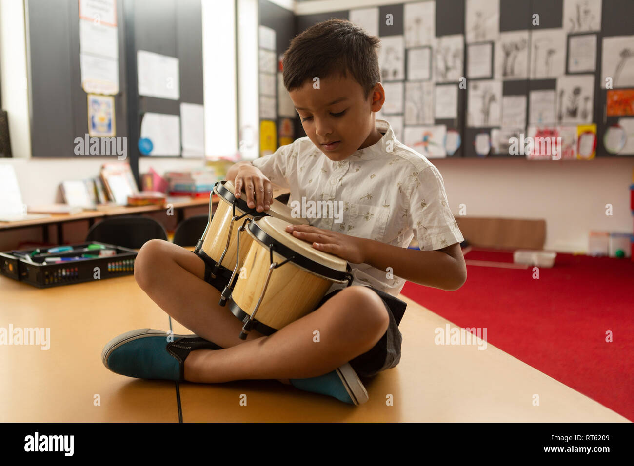 Schoolboy sitting on desk and playing bongo in a classroom Stock Photo ...