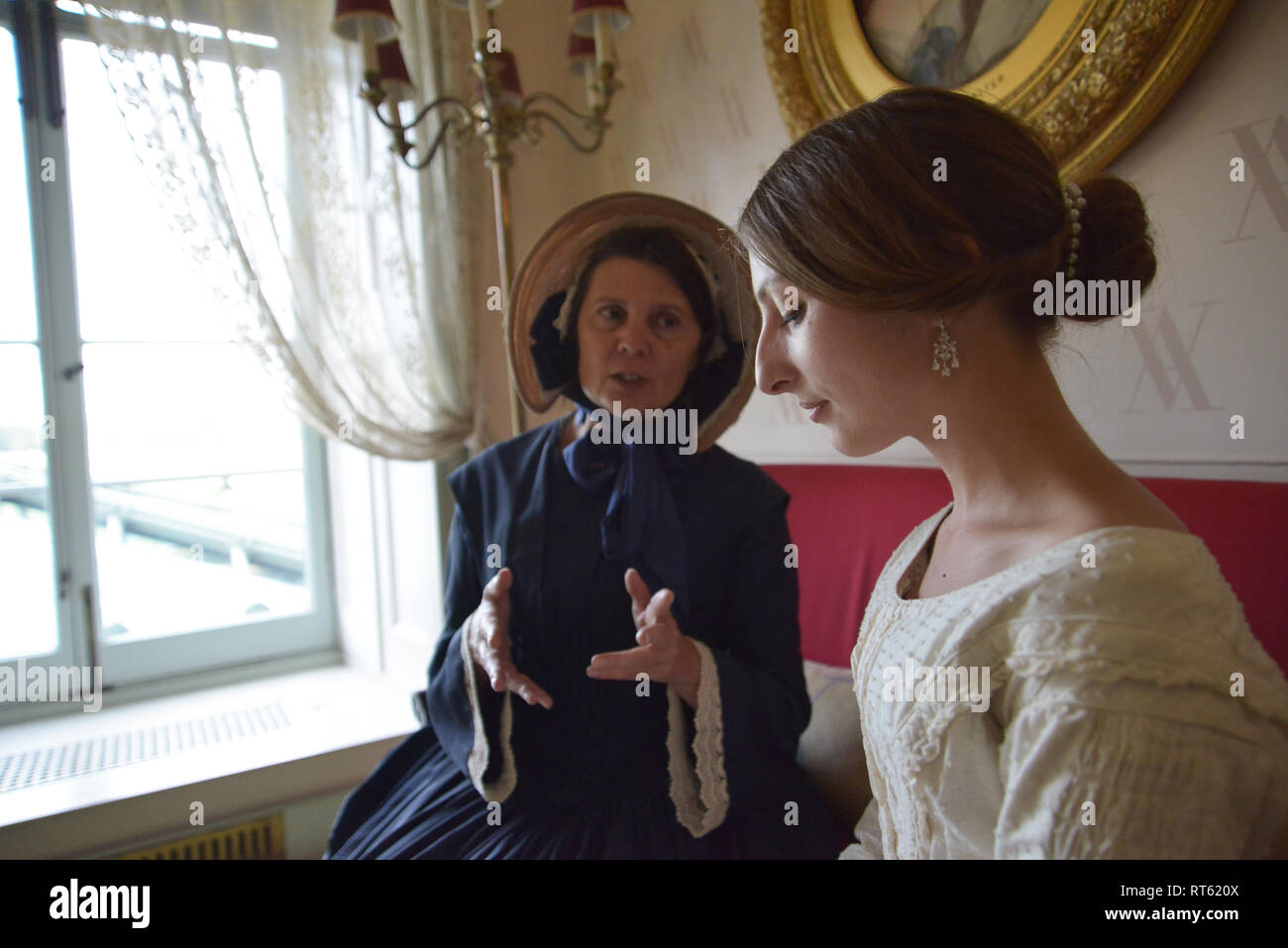 Two Women in Victorian dresses sit and chat in a formal parlour at ...
