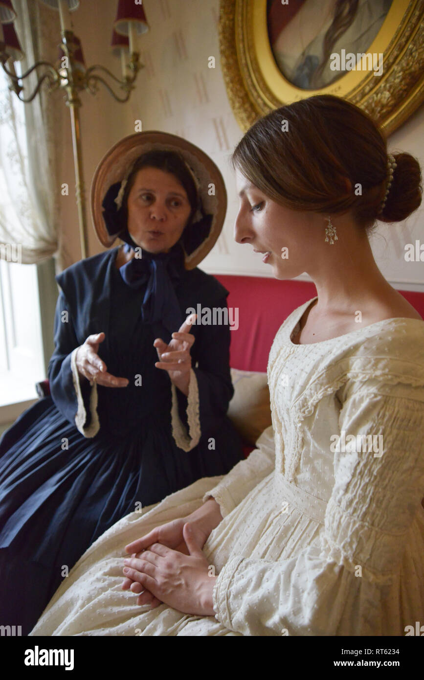 Two Women in Victorian dresses sit and chat in a formal parlour at ...