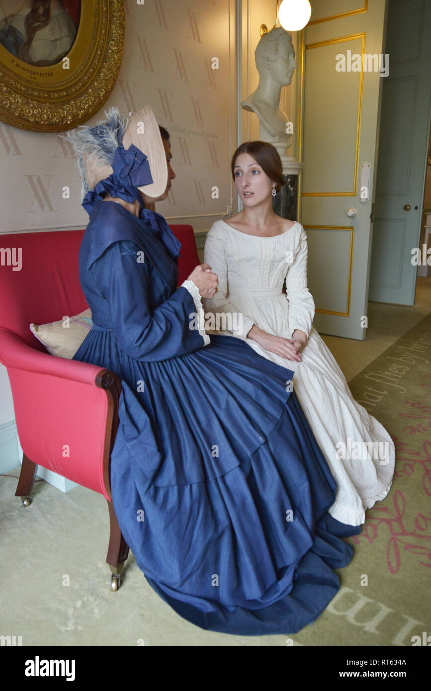 Two Women in Victorian dresses sit and chat in a formal parlour at ...