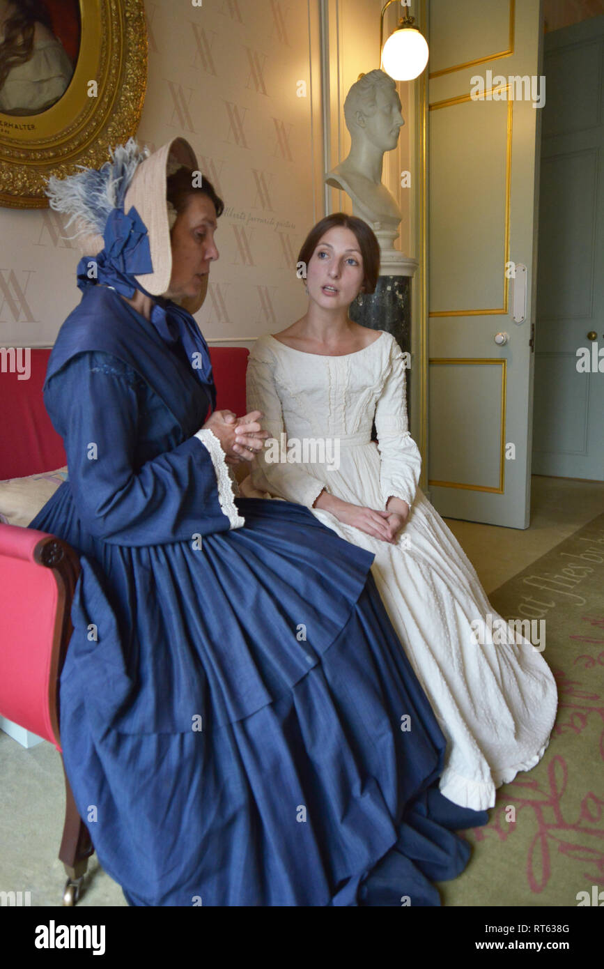 Two Women in Victorian dresses sit and chat in a formal parlour at ...
