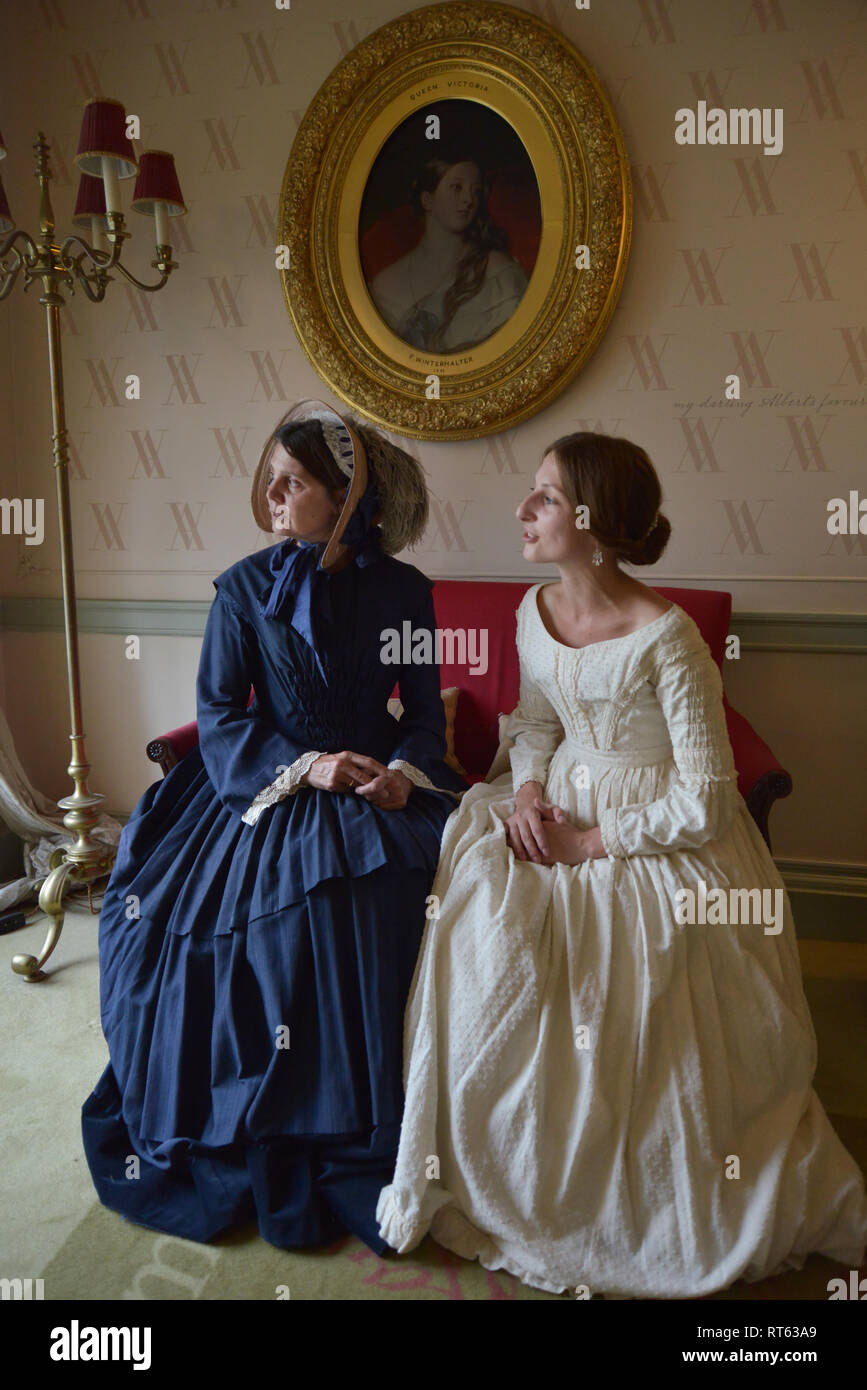 Two Women in Victorian dresses sit and chat in a formal parlour at ...