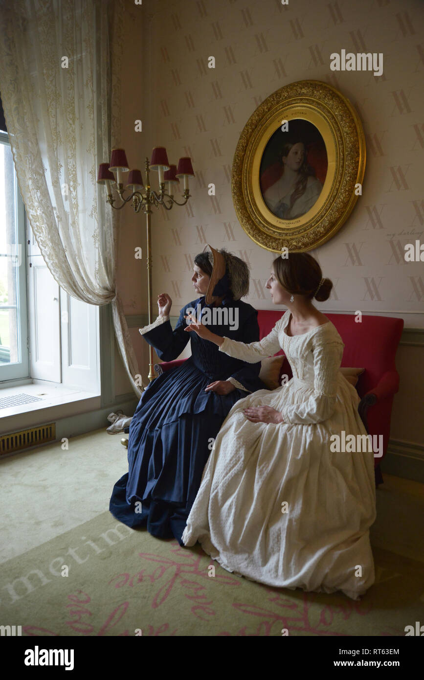 Two Women in Victorian dresses sit and chat in a formal parlour at ...