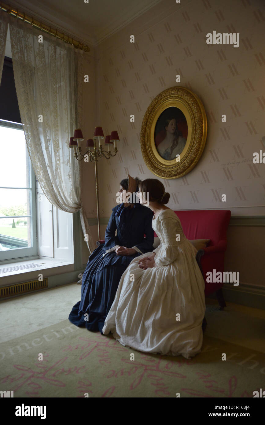 Two Women in Victorian dresses sit and chat in a formal parlour at ...