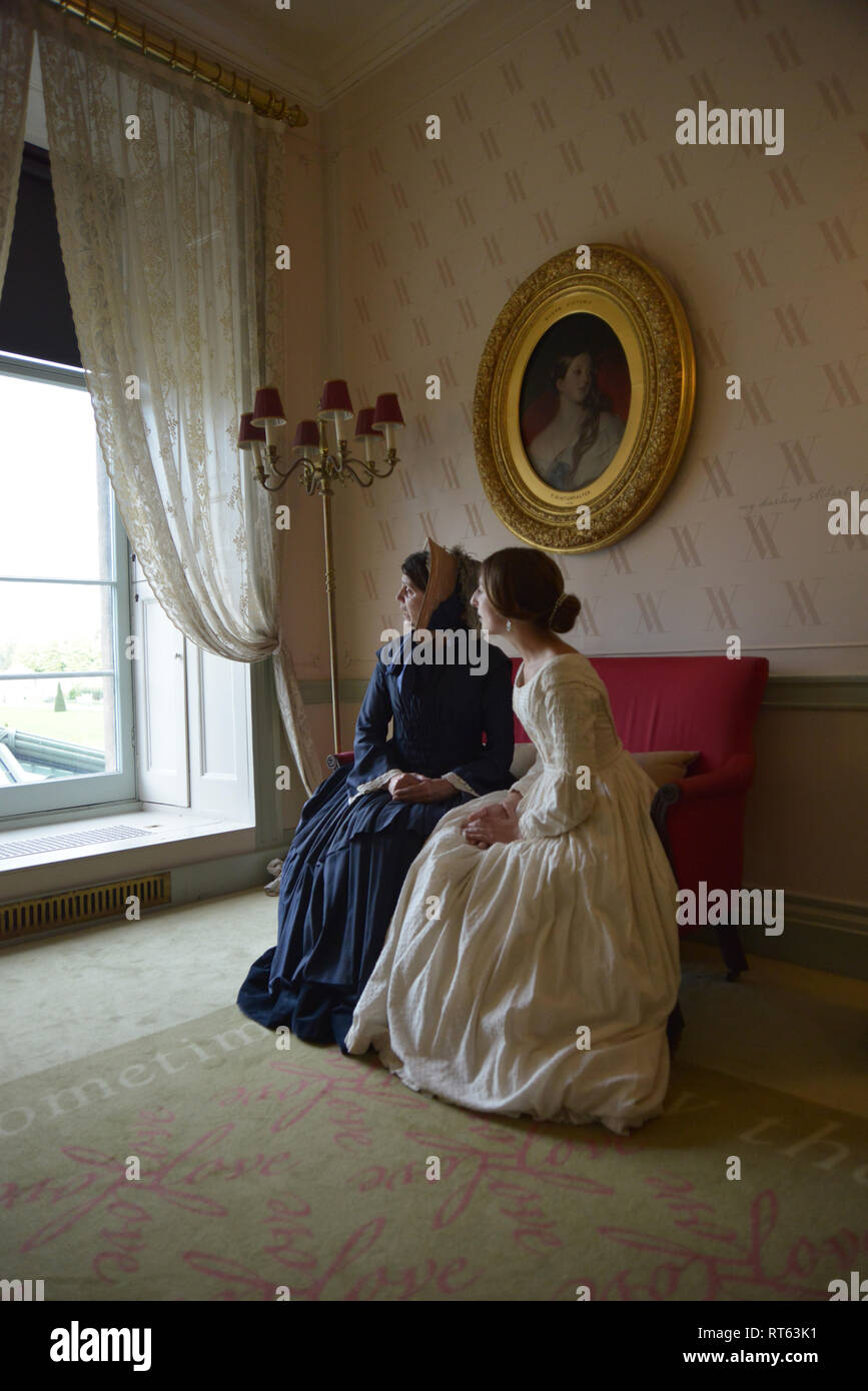 Two Women in Victorian dresses sit and chat in a formal parlour at ...