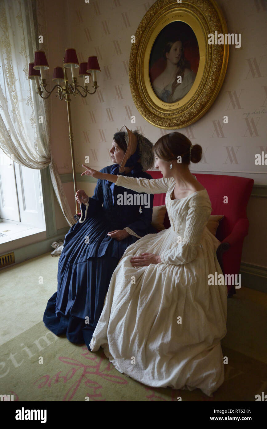 Two Women in Victorian dresses sit and chat in a formal parlour at ...