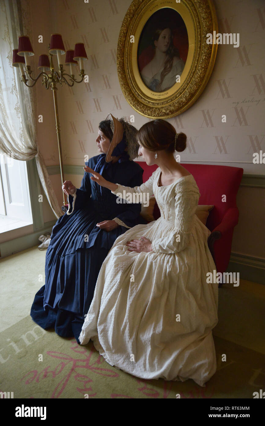 Two Women in Victorian dresses sit and chat in a formal parlour at ...