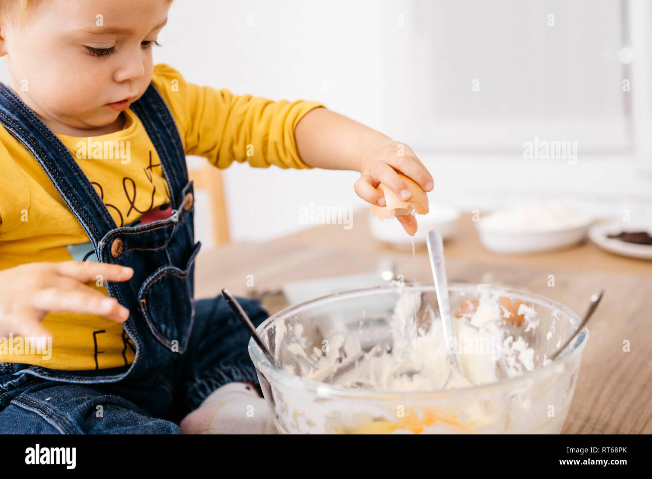 Toddler girl sitting on kitchen table throwing egg into bowl for ...