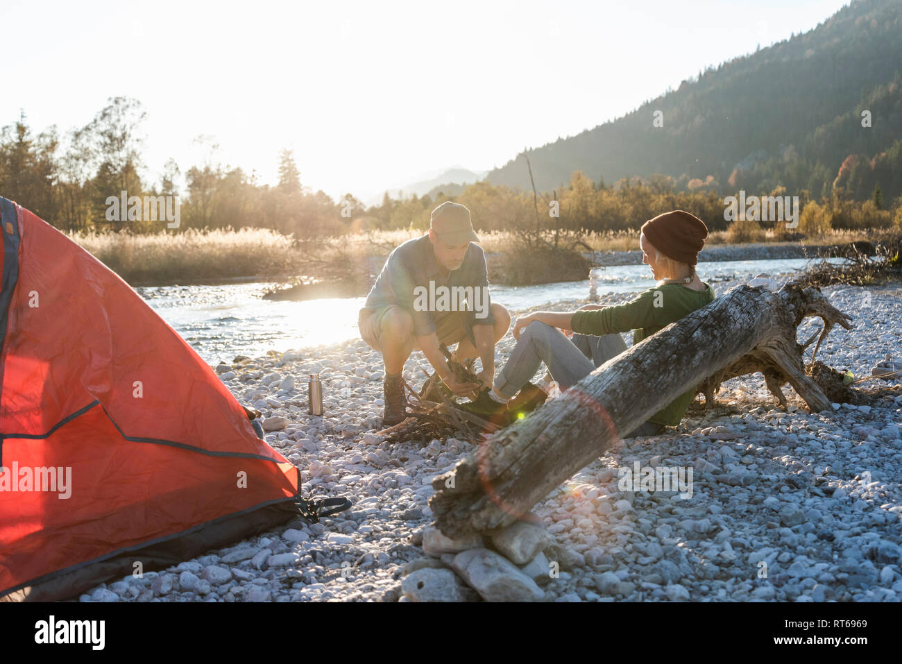Mature Couple Camping At Riverside Collecting Wood For A Camp Fire