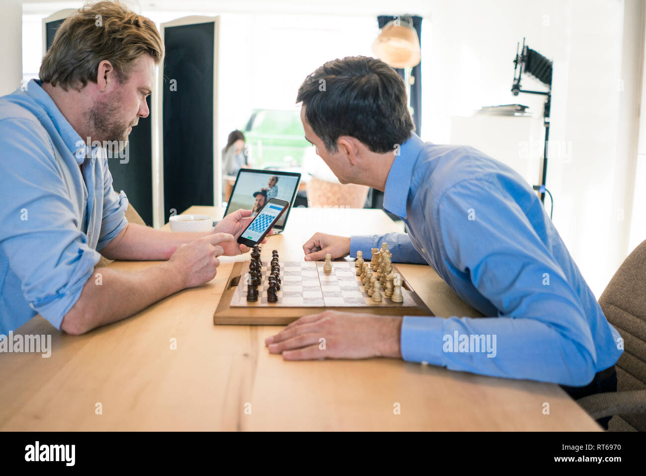 Two men playing chess and checking smartphone Stock Photo - Alamy