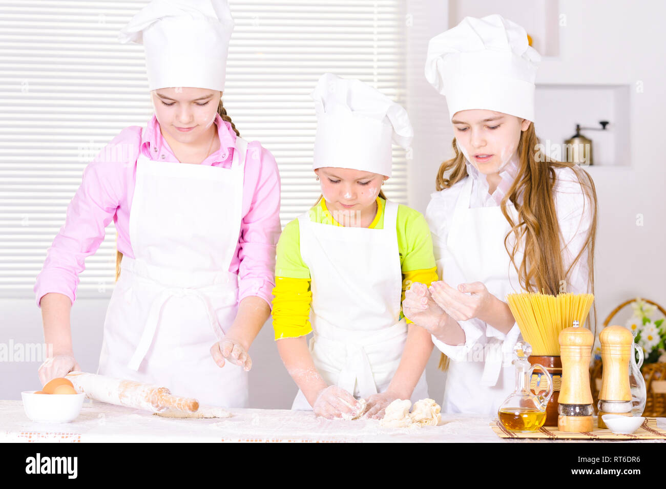 Portrait of three cute girls cooking on kitchen Stock Photo - Alamy
