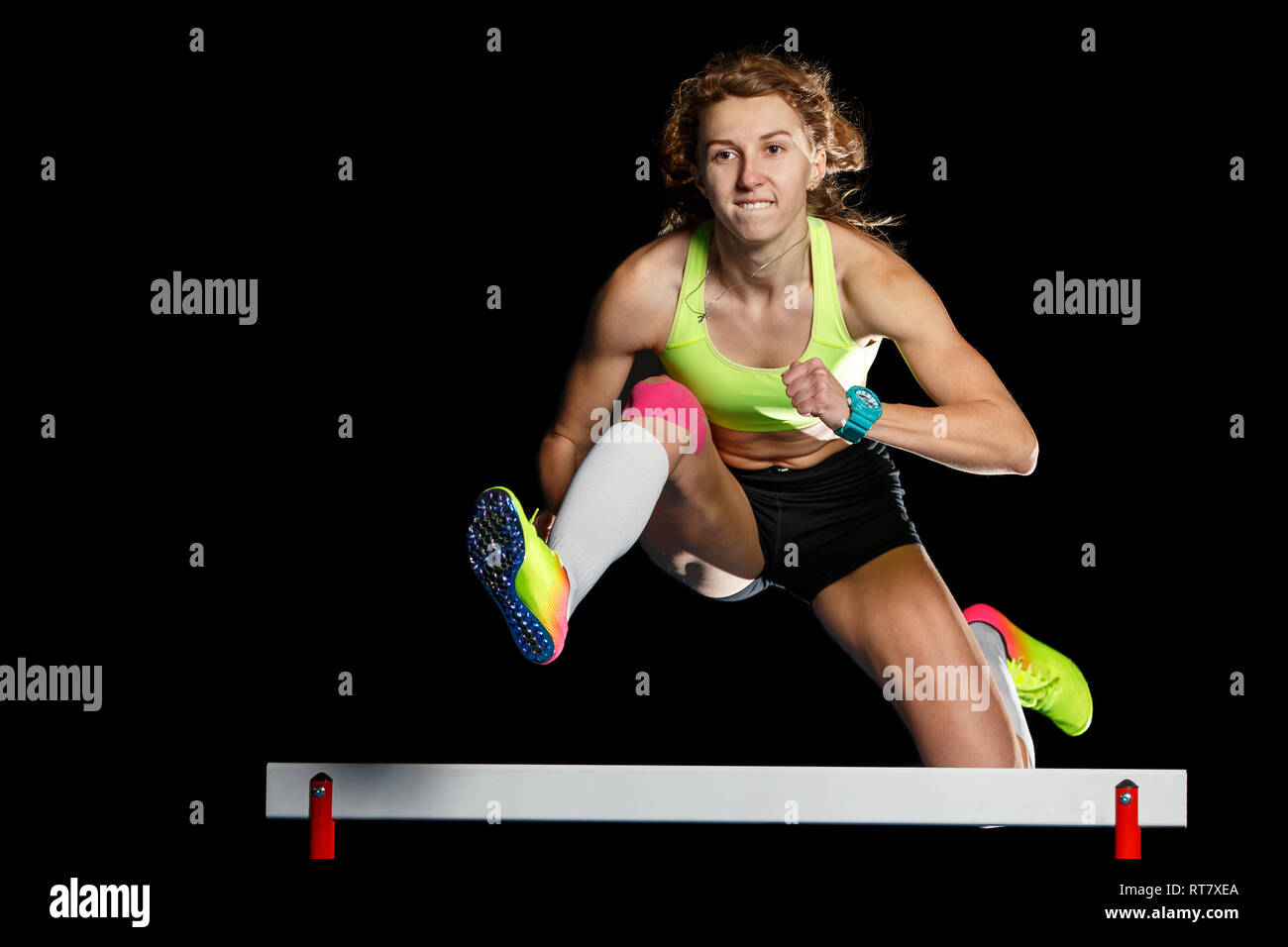 Young female athlete jumping over hurdle in sprint. Sprinter jumping ...