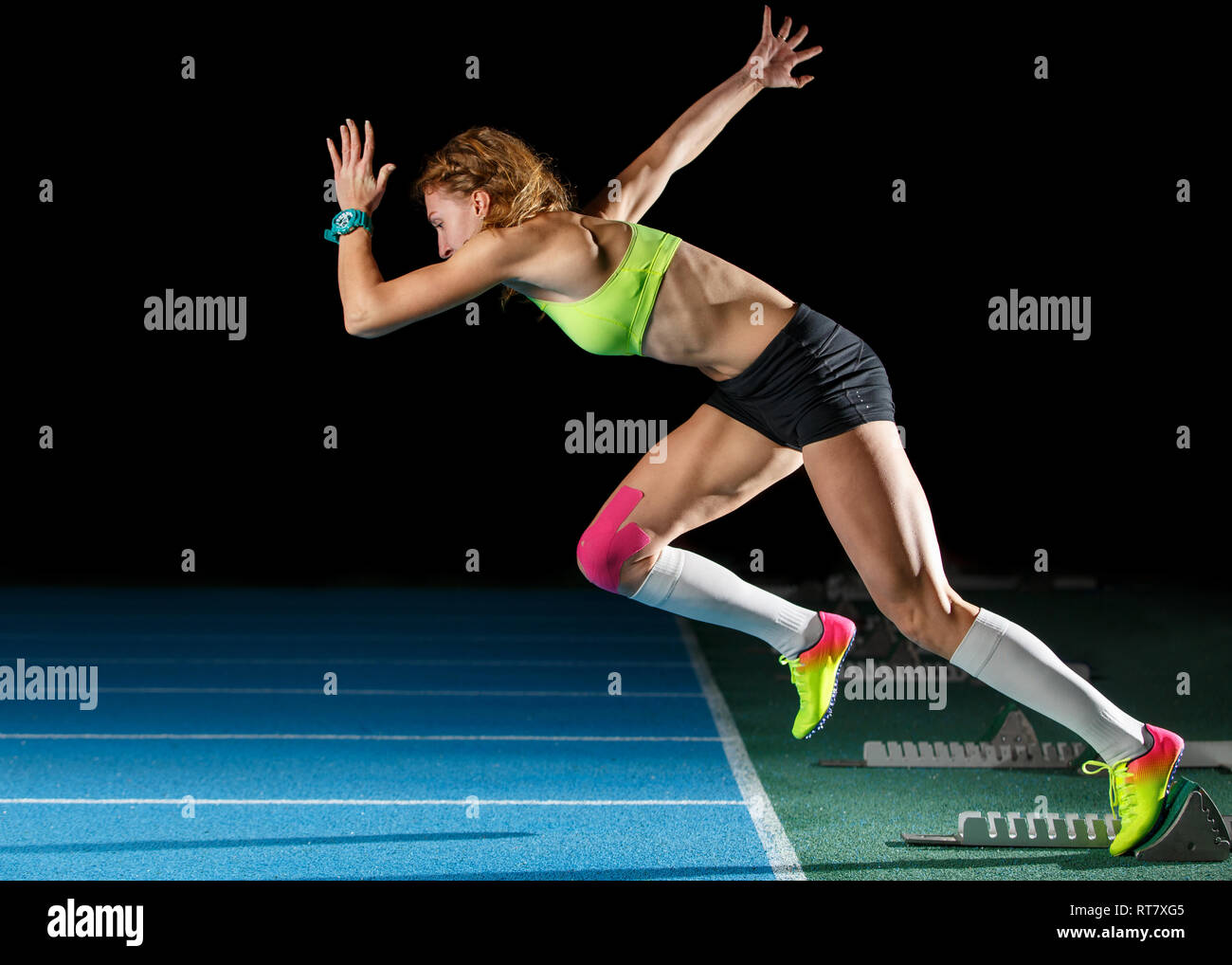 Female athlete starting sprint race running from blocks against black ...