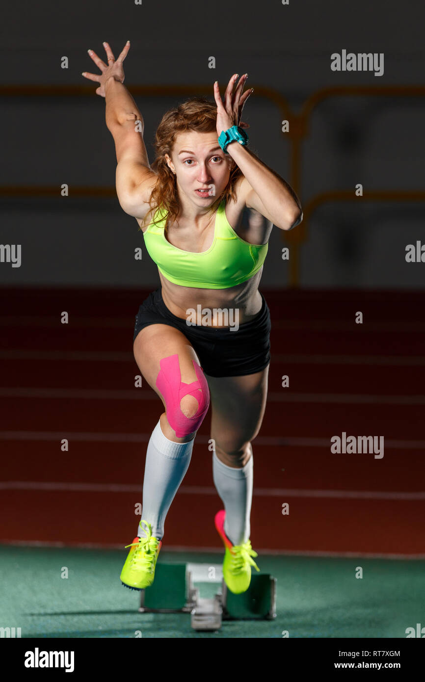 Female athlete starting sprint race running from blocks against dark ...