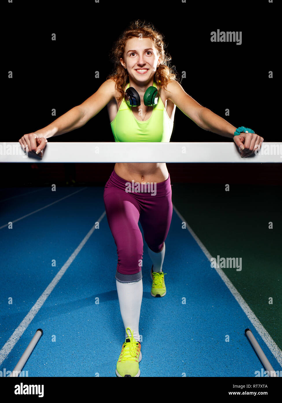 Young smiling female athlete standing near hurdle on sprint lane ...