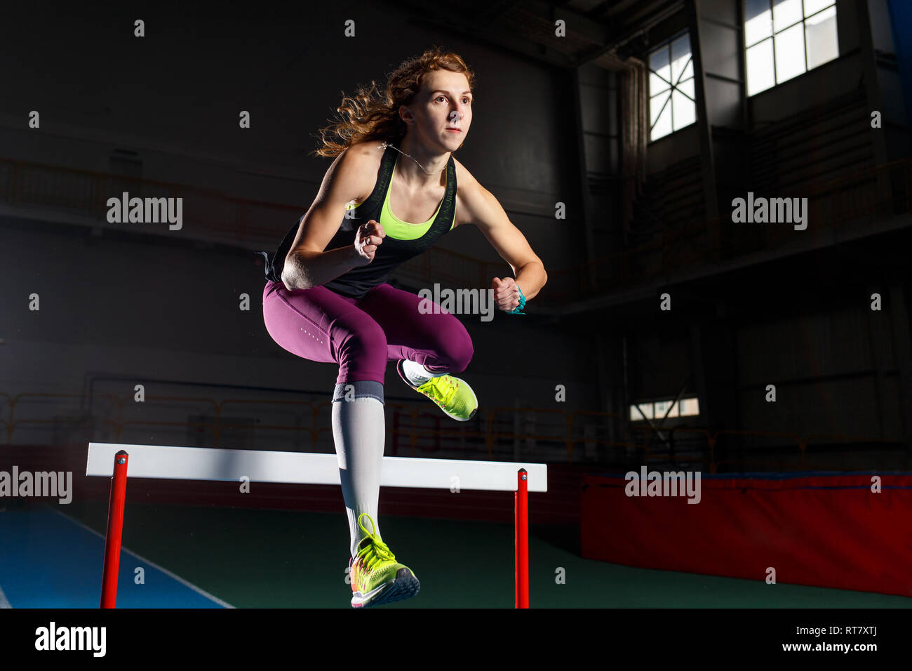 Young sportswoman running and jumping over a hurdle. Sprint race with ...