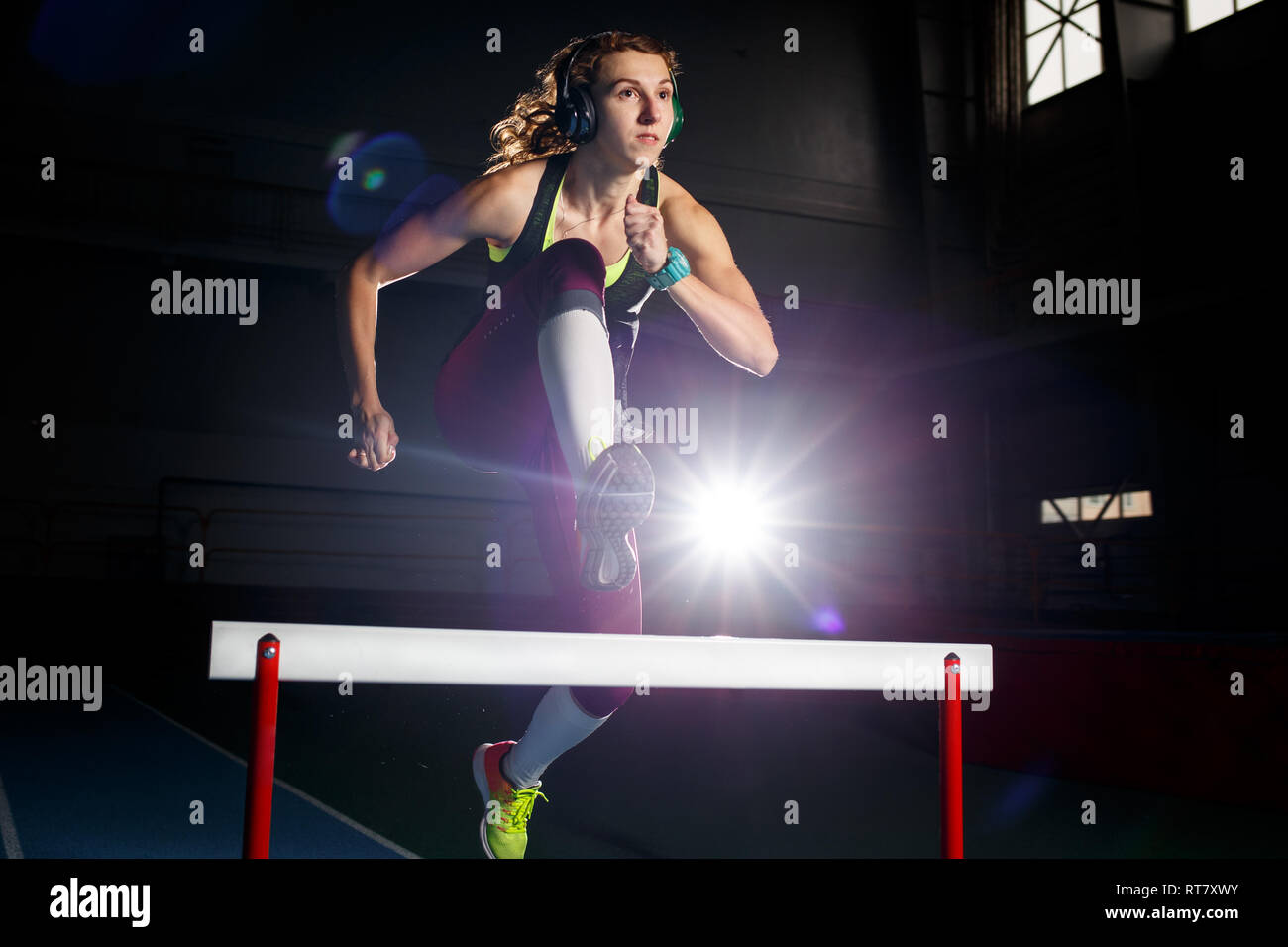 Young sportswoman running and jumping over a hurdle. Sprint race with ...