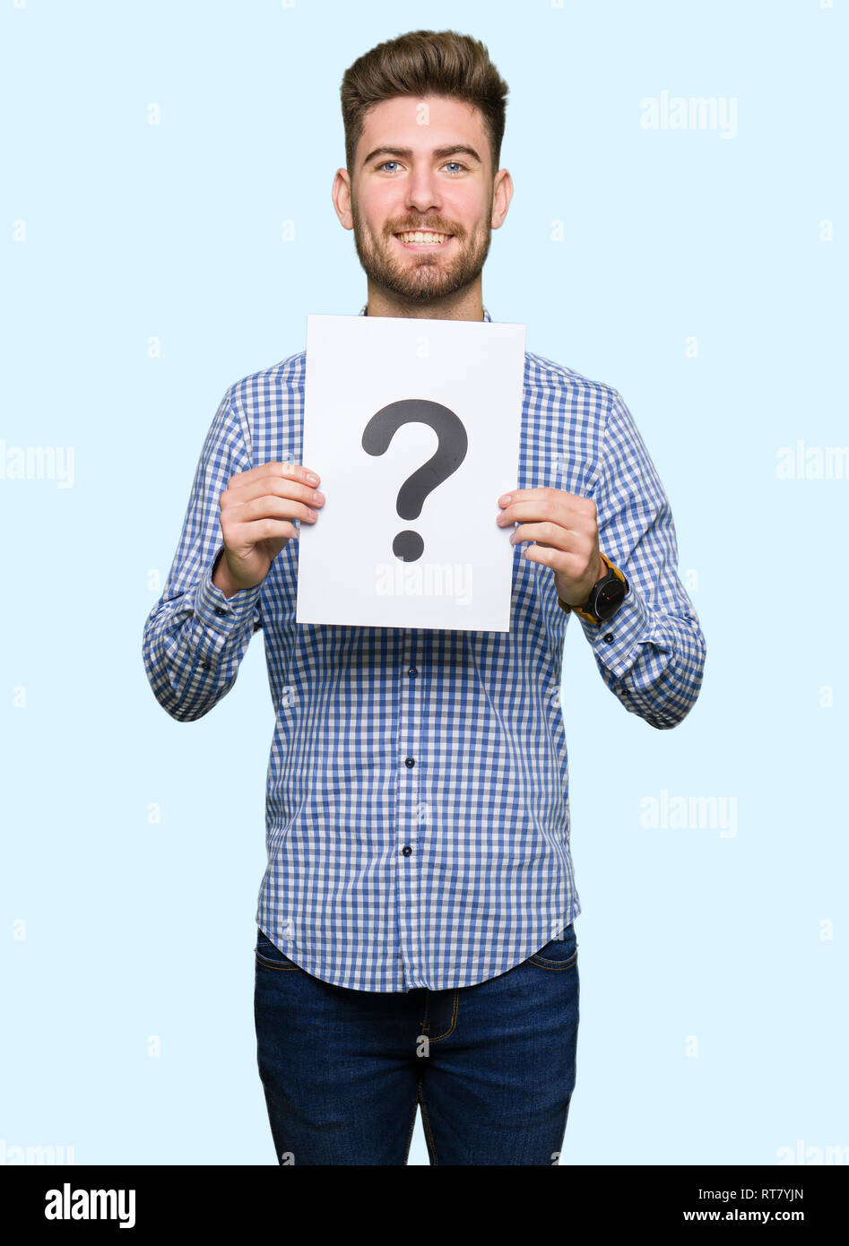 Young handsome man holding paper with question mark with a happy face ...