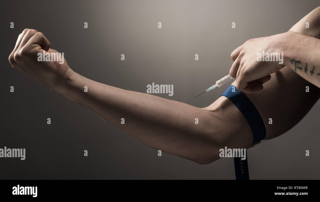 partial view of addict man making injection of heroin dose on grey ...