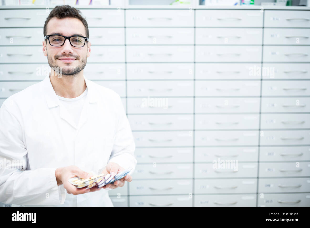 Portrait of smiling pharmacist holding tablet packages at cabinet in ...