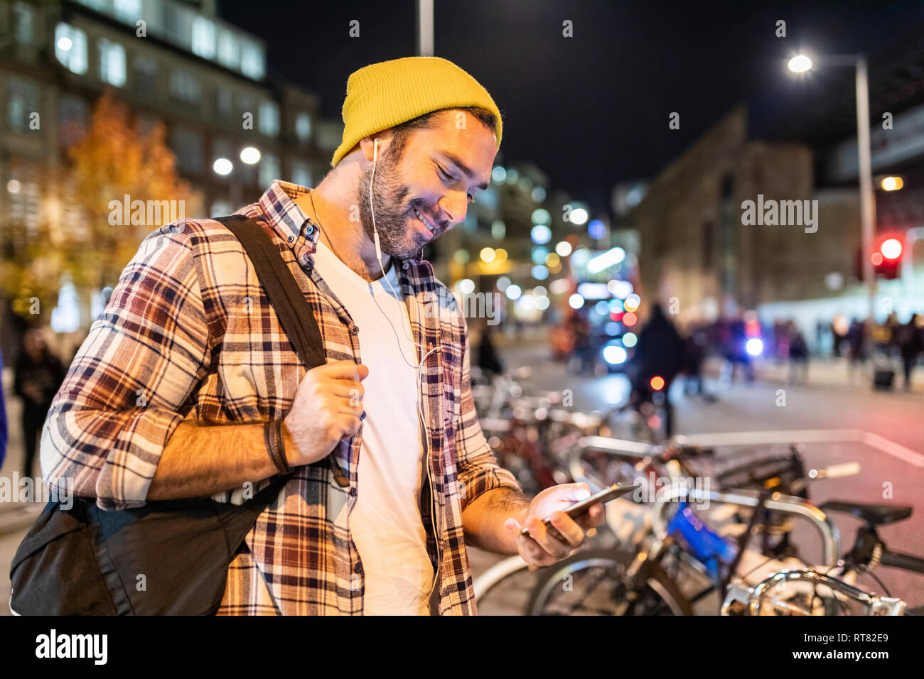 UK, London, man commuting at night in the city and looking at his phone ...