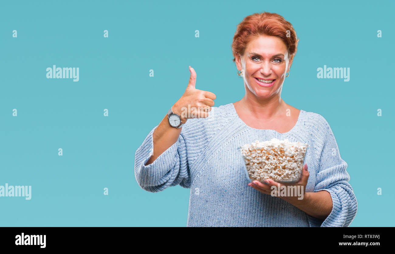 Atrractive senior caucasian redhead woman eating popcorn over isolated ...