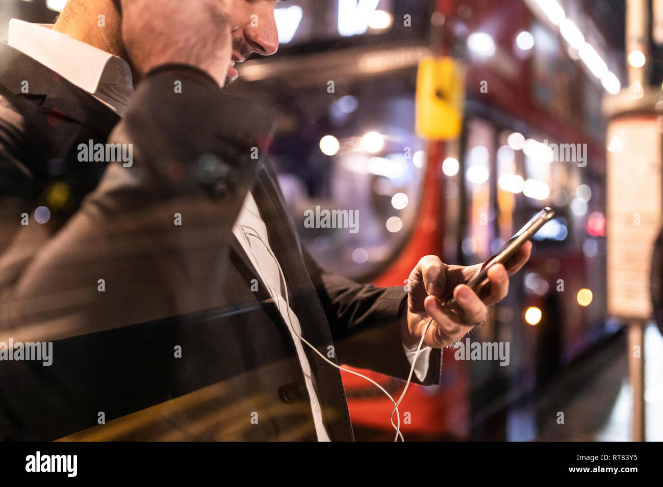 UK, London, businessman with cell phone and earbuds at the bus station ...