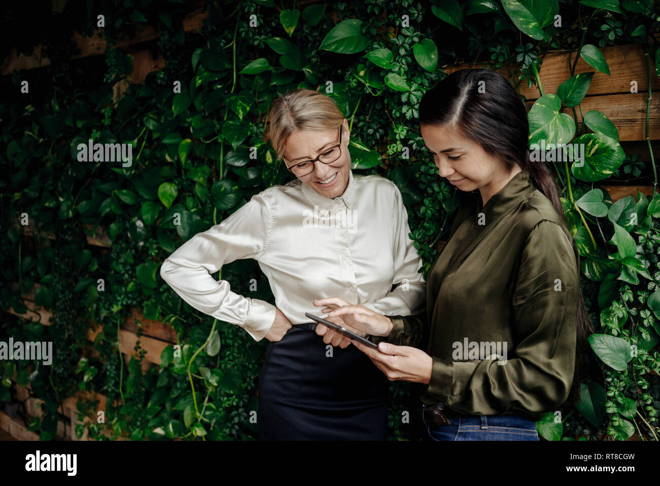 Two businesswomen in green office looking at tablet Stock Photo - Alamy