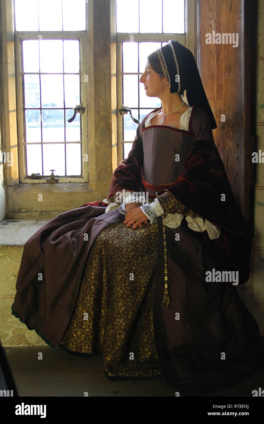 A beautiful young Woman dressed as Anne Boleyn sits by a window at the ...
