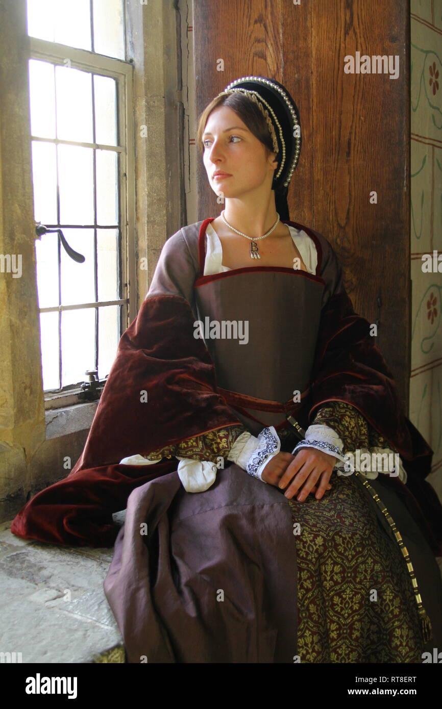 A beautiful young Woman dressed as Anne Boleyn sits by a window at the ...
