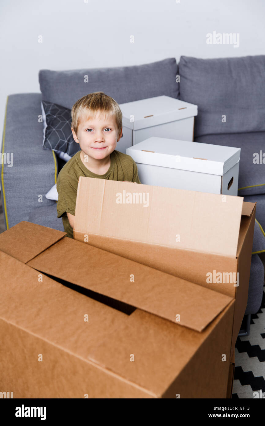 Boy sits among cardboard boxes on floor against gray sofa Stock Photo ...