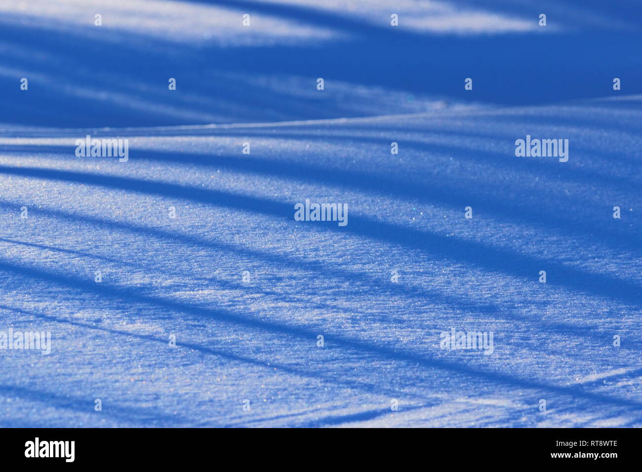 The wind has formed patterns in the snow covering a frozen lake. The ...