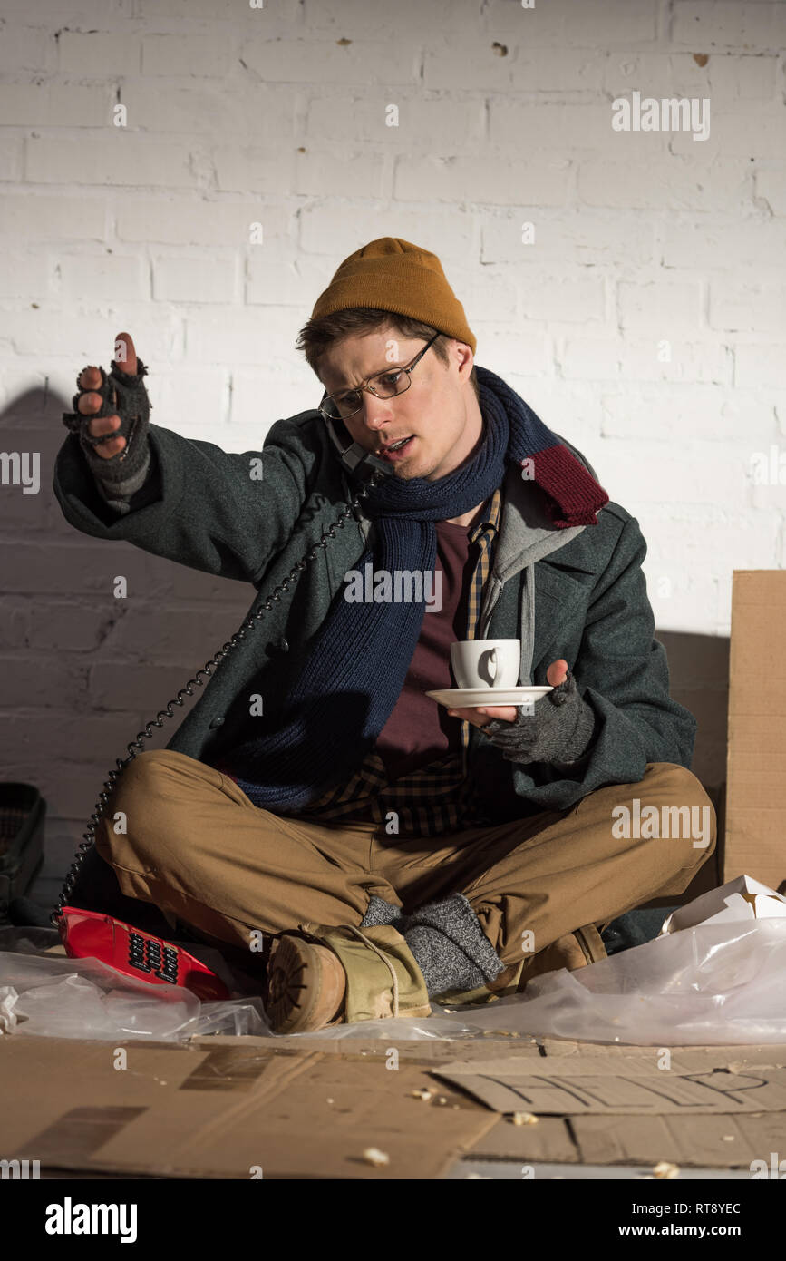 homeless man holding coffee cup and using vintage phone Stock Photo - Alamy