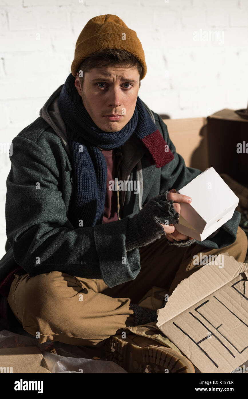 sad homeless man sitting with cardboard card with "help" lettering and ...