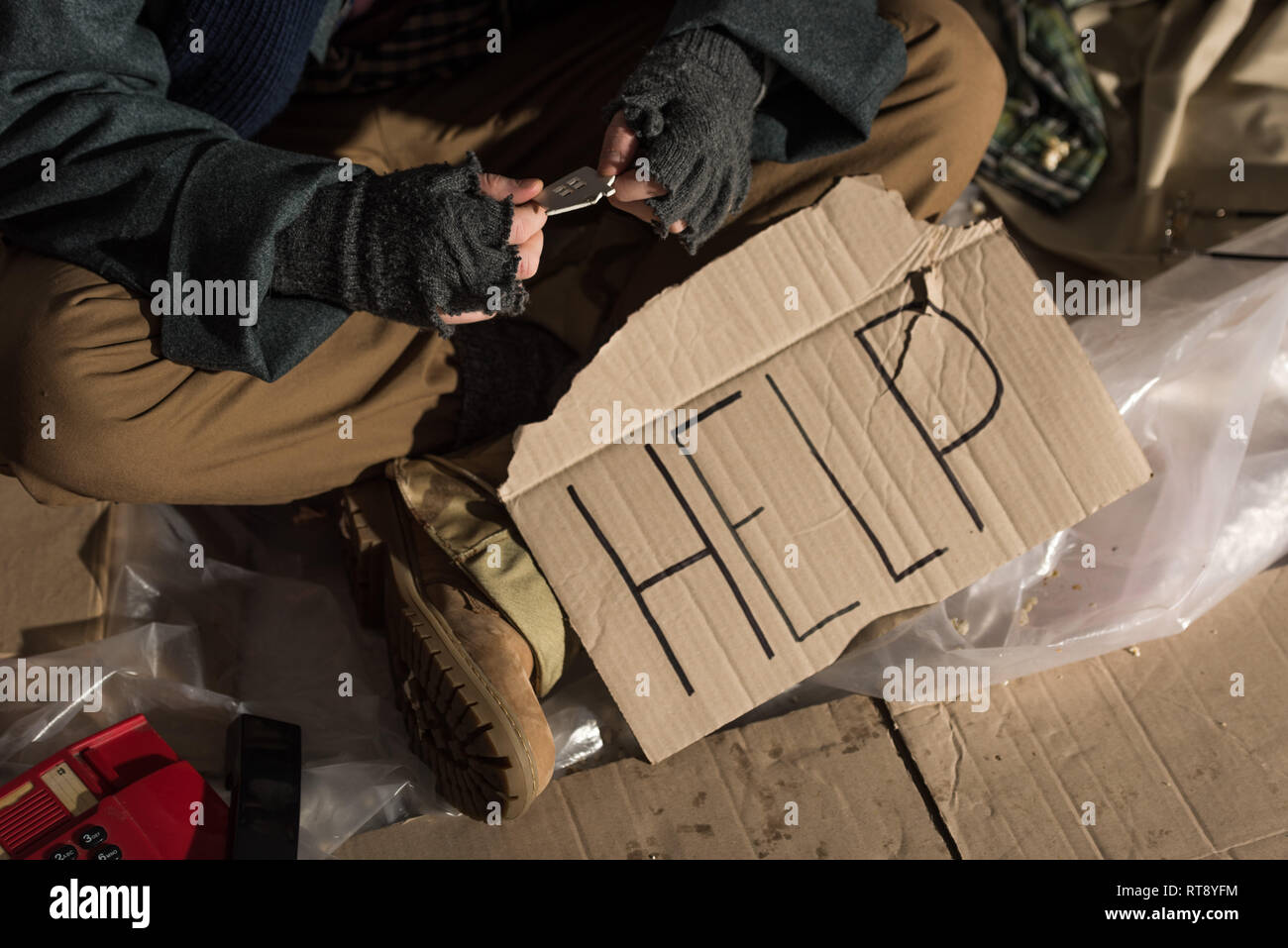 cropped view of homeless man sitting with cardboard card with "help ...