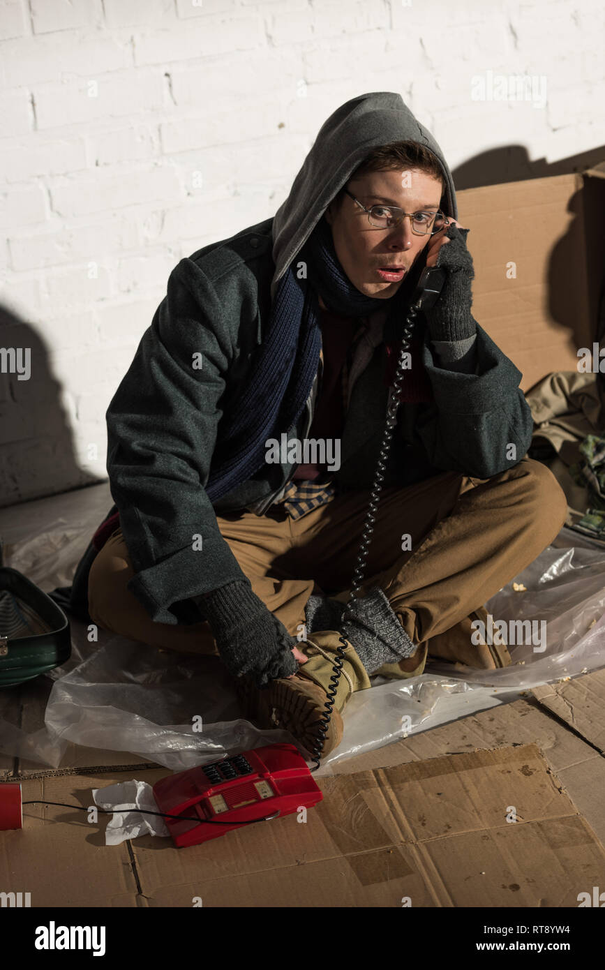 homeless man in hood and glasses grimacing while using vintage phone ...