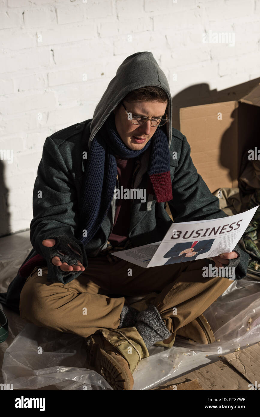 surprised homeless man reading business newspaper while sitting on ...