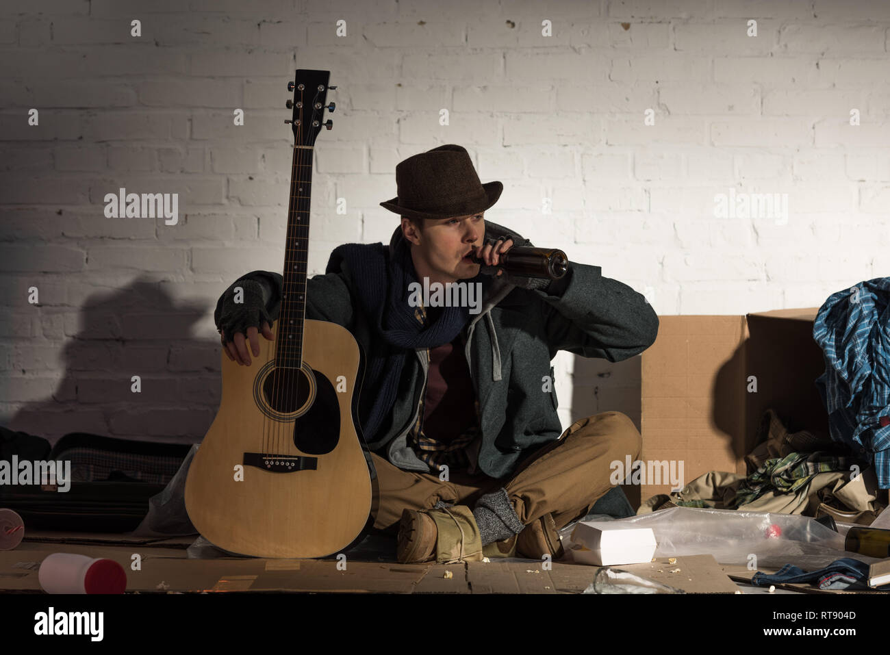homeless man holding guitar and drinking from alcohol bottle while ...