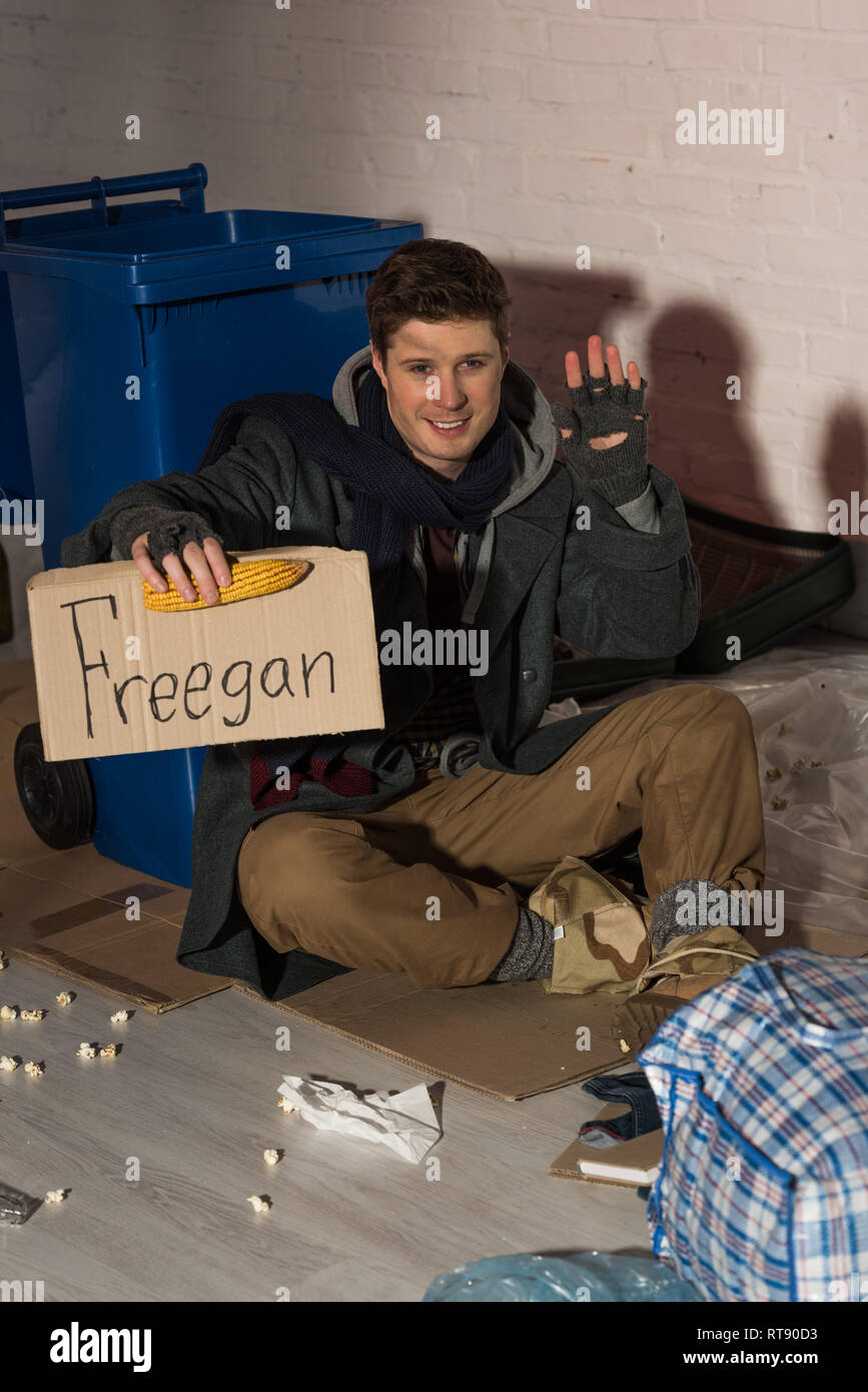 smiling homeless man waving hand while holding cardboard card with ...