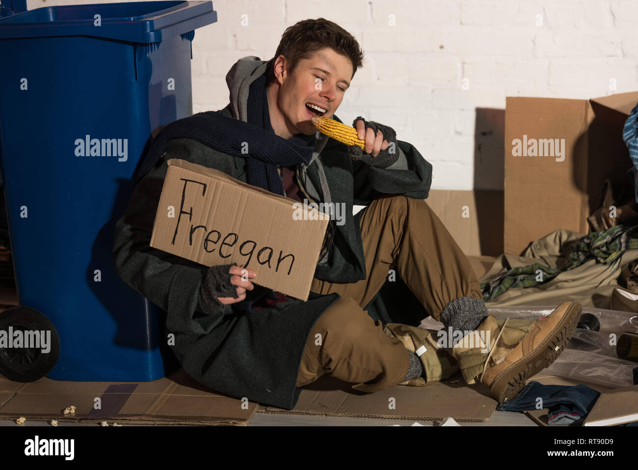 homeless man eating corn cob and holding cardboard card with "freegan ...