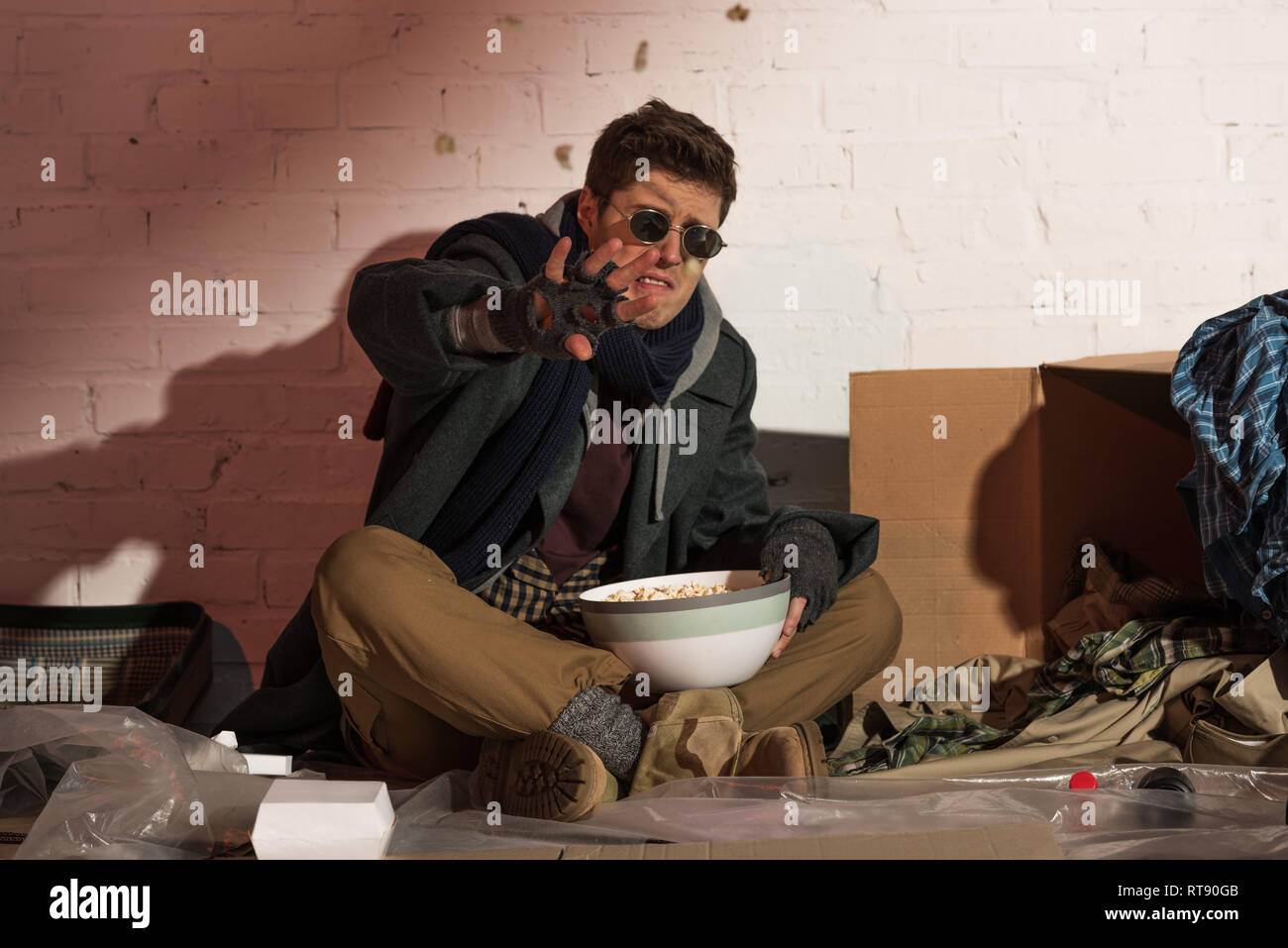 homeless man sitting on garbage dump and throwing popcorn from bowl ...