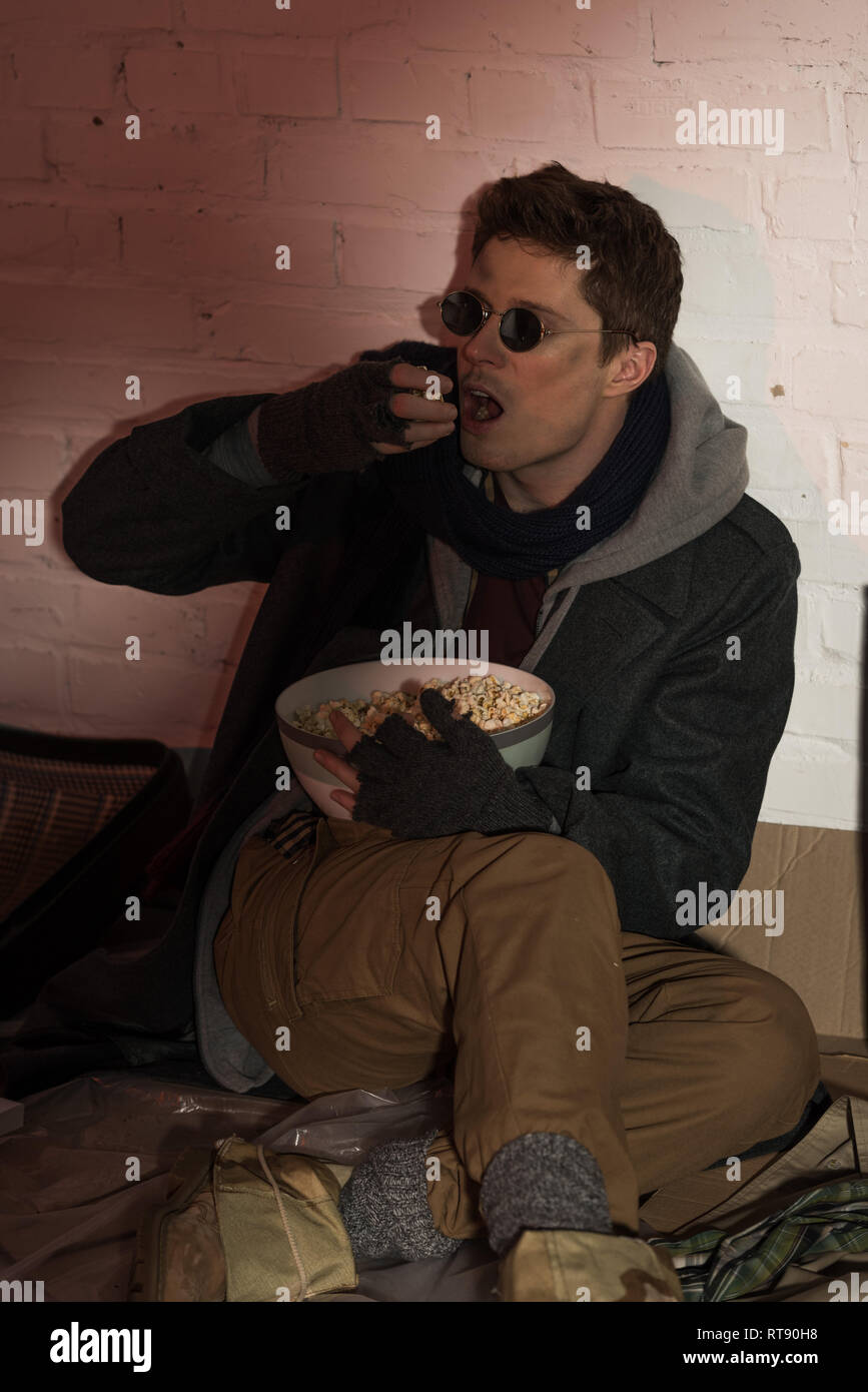 hungry homeless man siting by brick wall and eating popcorn Stock Photo ...