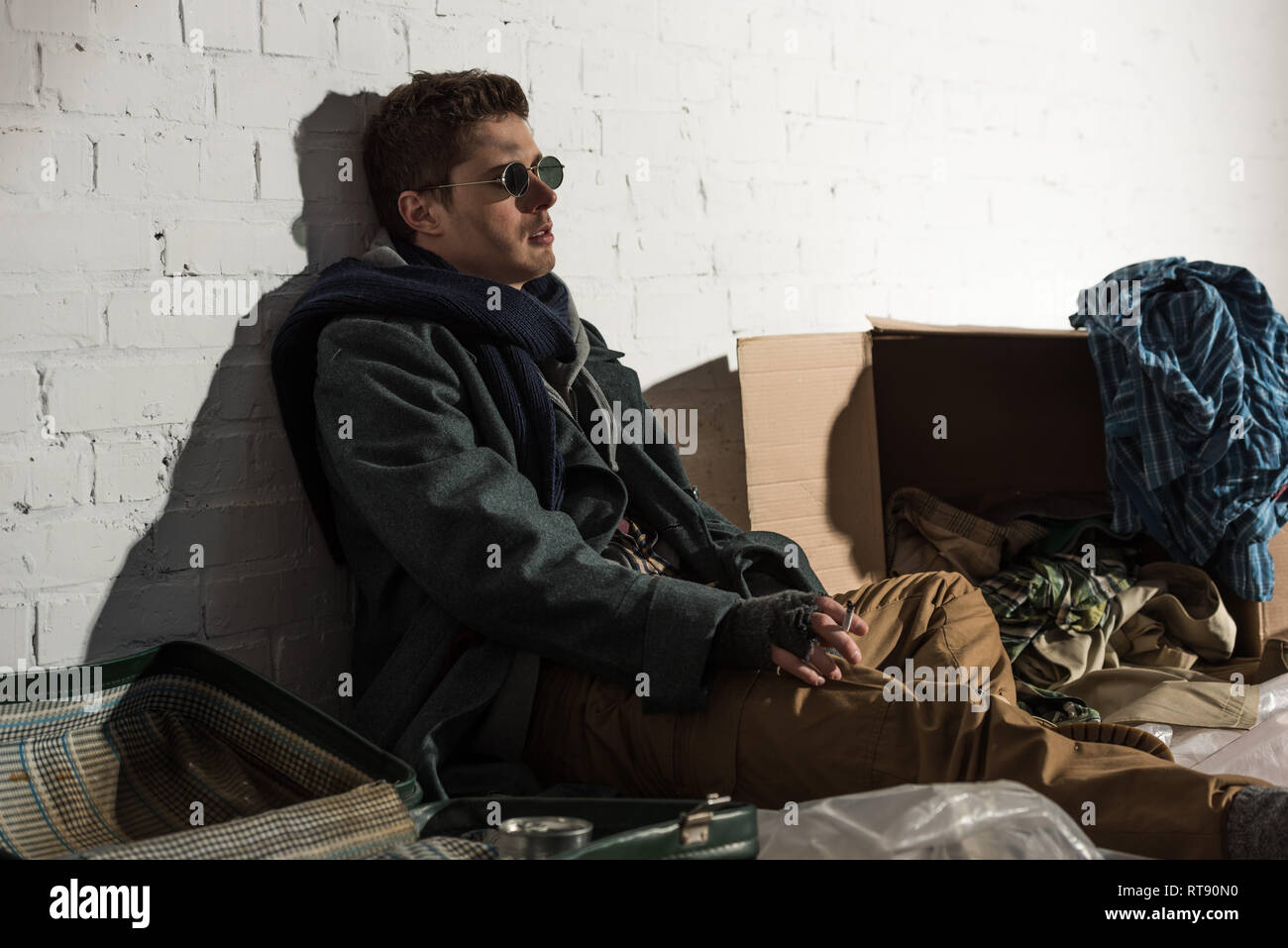 homeless man smoking while sitting by white brick wall Stock Photo - Alamy