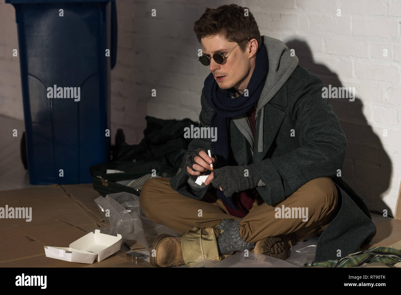homeless man sitting on rubbish damp and holding cigarette Stock Photo ...