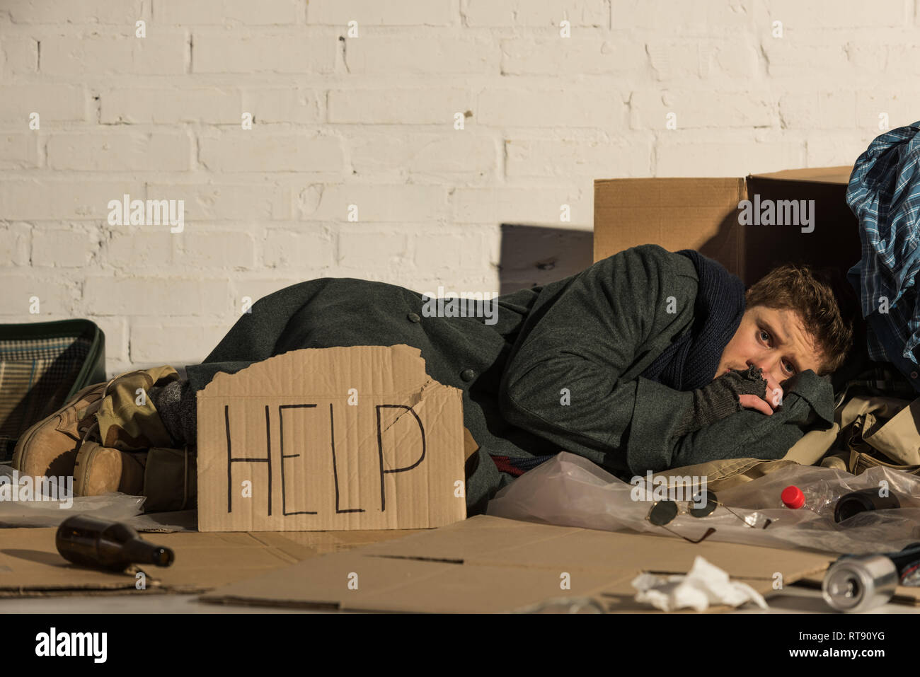 homeless misery man with "help" inscription card lying on cardboard ...