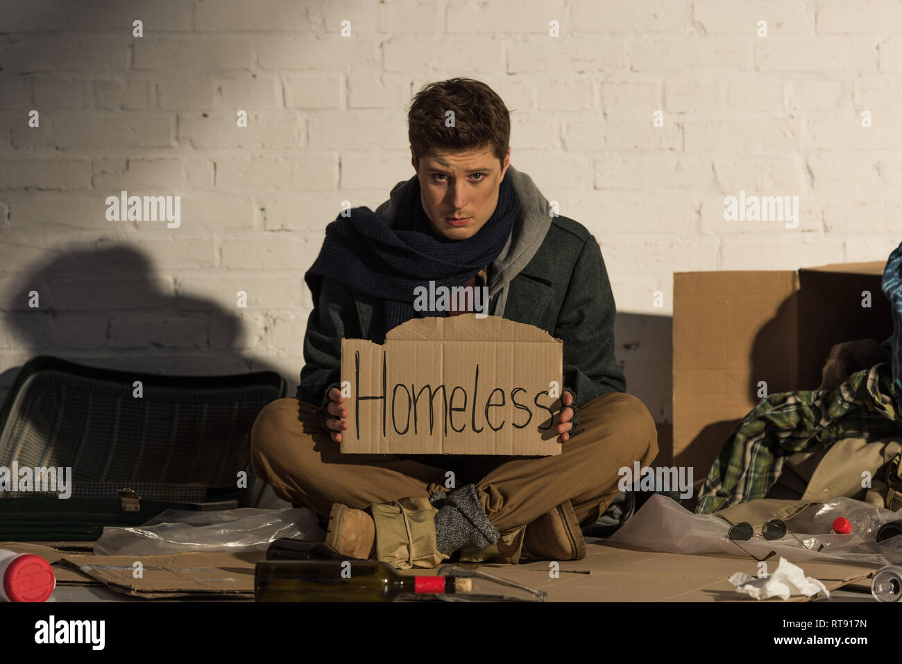 sad man sitting on rubbish dump and holding cardboard card with ...