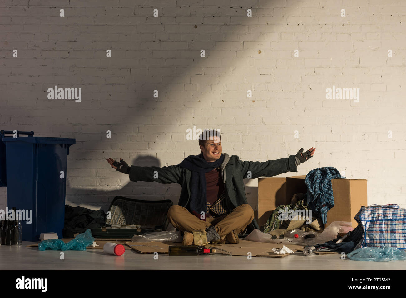 smiling homeless man sitting on cardboard surrounded by rubbish and ...